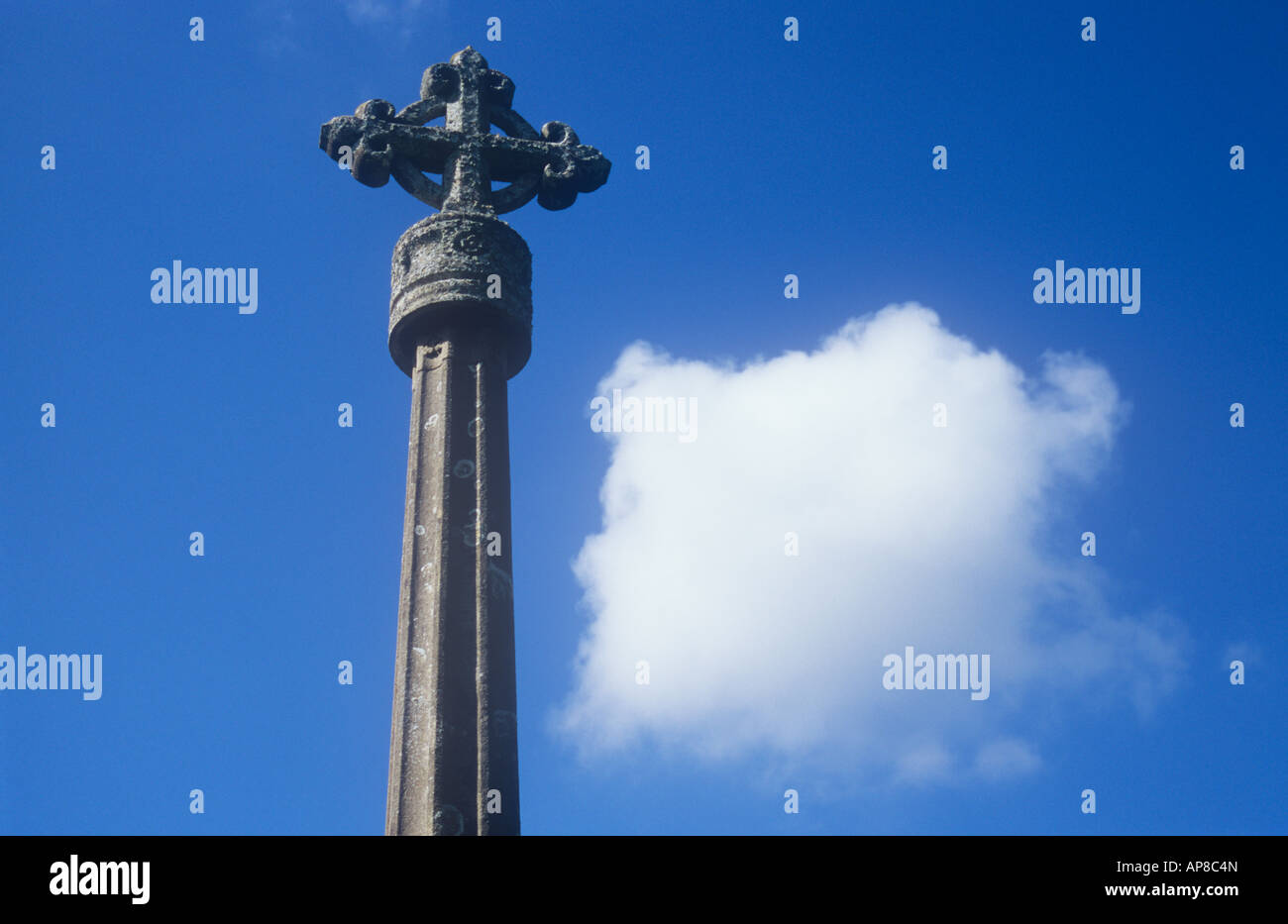 Lichen-covered stone Celtic cross on top of stone pillar against deep ...