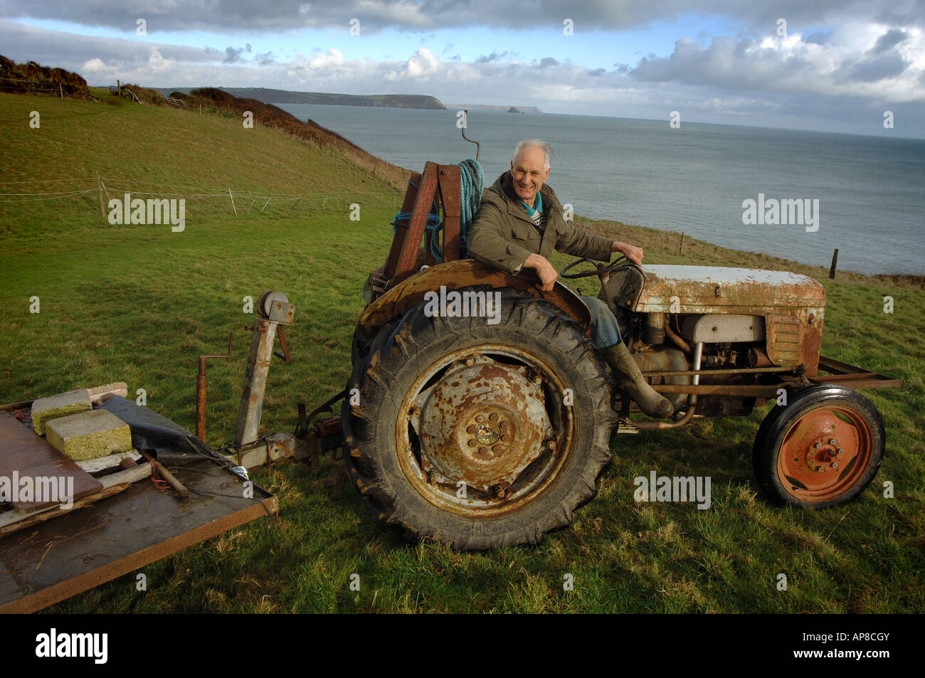 An old aged farmer sitting on an old tractor in a field over looking ...