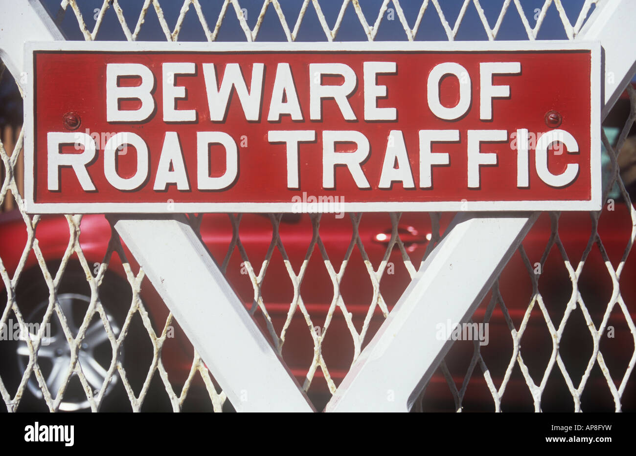 Bold metal sign painted white on scarlet red on gate with red car ...