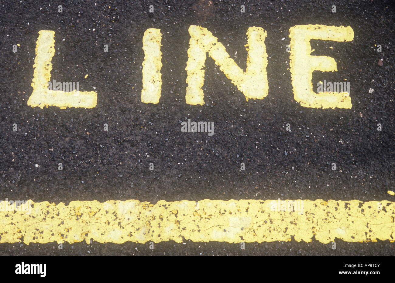 Pale yellow line painted on black tarmac and above it the painted word ...