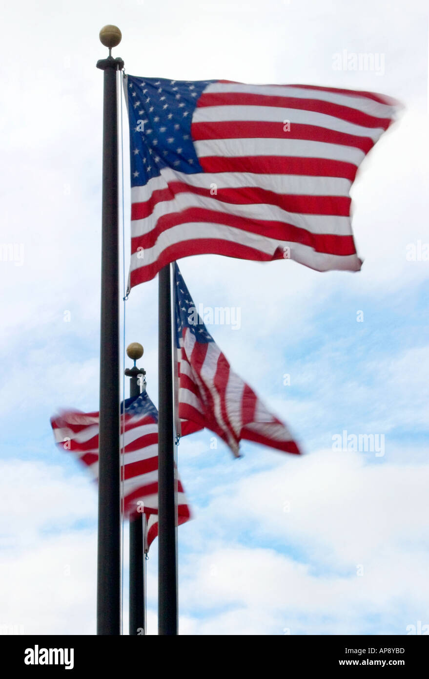 Three American flags flying against a blue sky with puffy white clouds ...