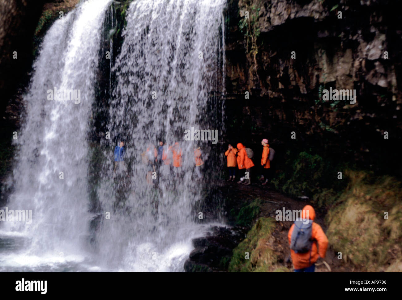 Students on geography fieldwork explore the overhang of a waterfall ...