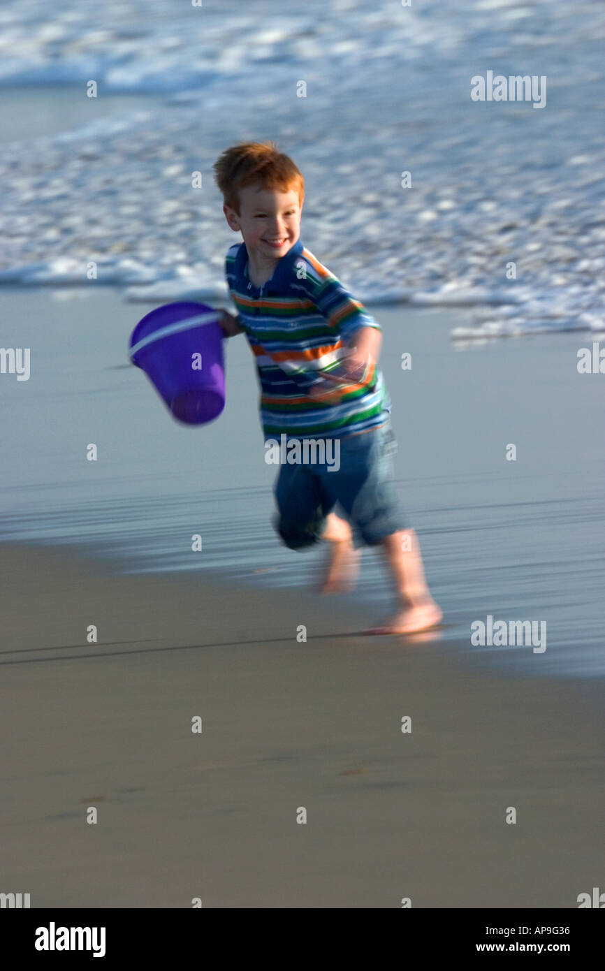 An appealing young boy runs from the waves while playing at the beach ...
