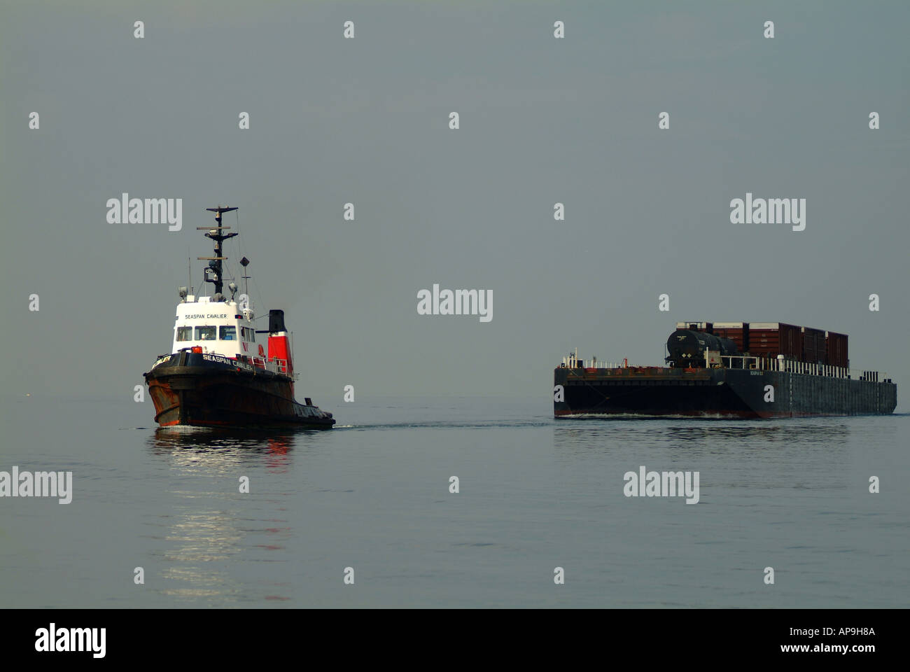 Tug boat towing a barge on open flat water Stock Photo - Alamy