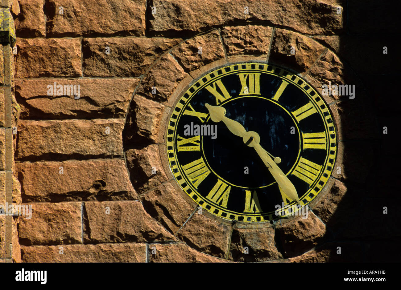 Shadow falling on brown sandstone brick wall with round analogue clock ...