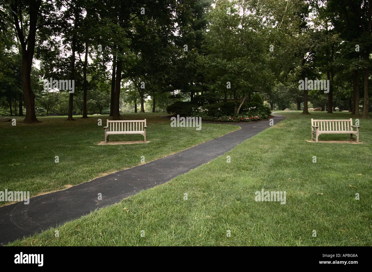two park benches in a grassy wooded park with a paved path going ...