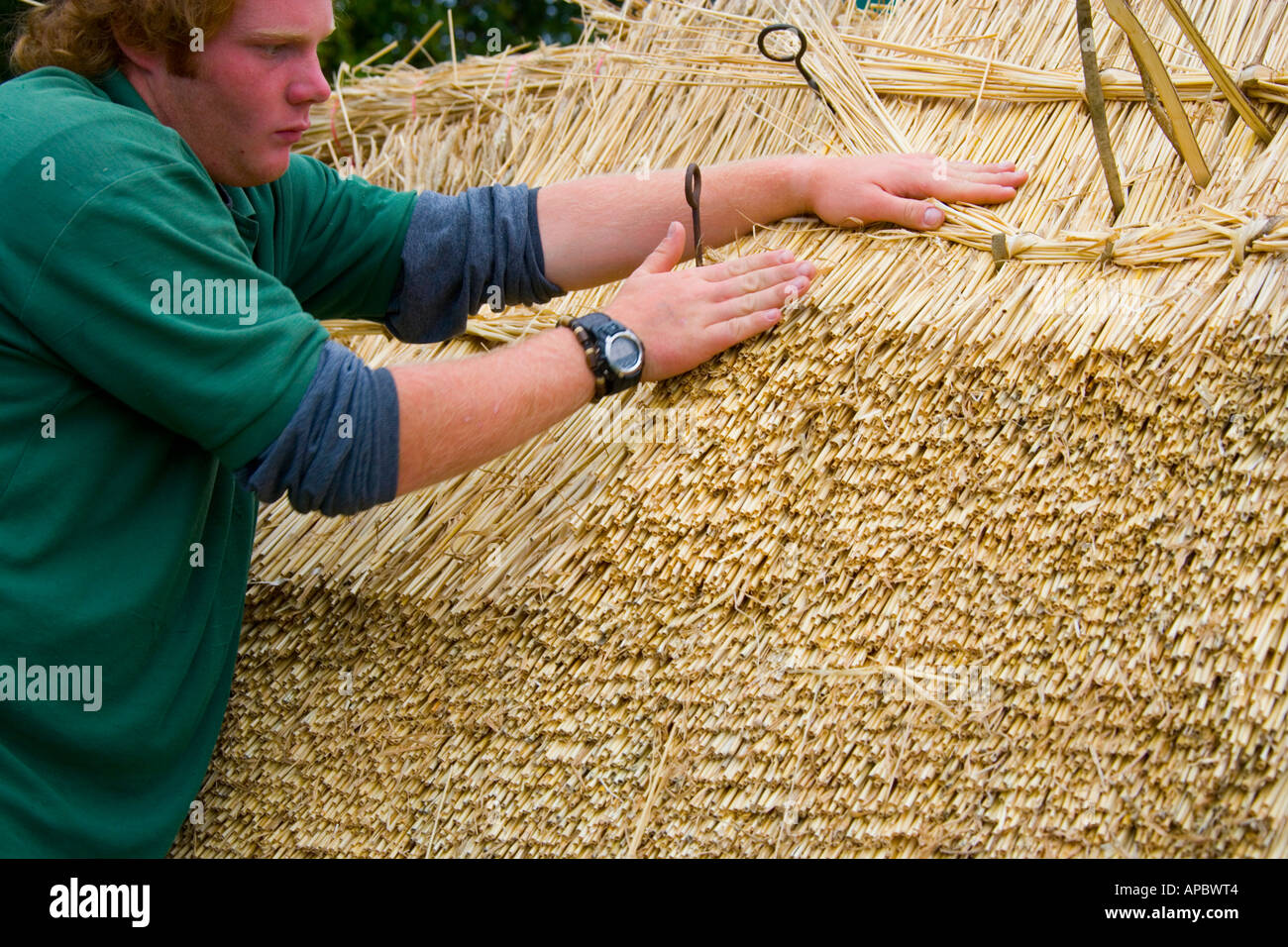 Close up of thatcher at work on roof finalising position of reeds ...
