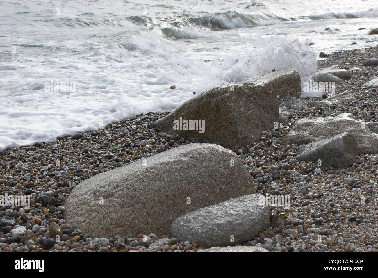 Close up of sea washing ashore on a shingle beach with bolders in ...