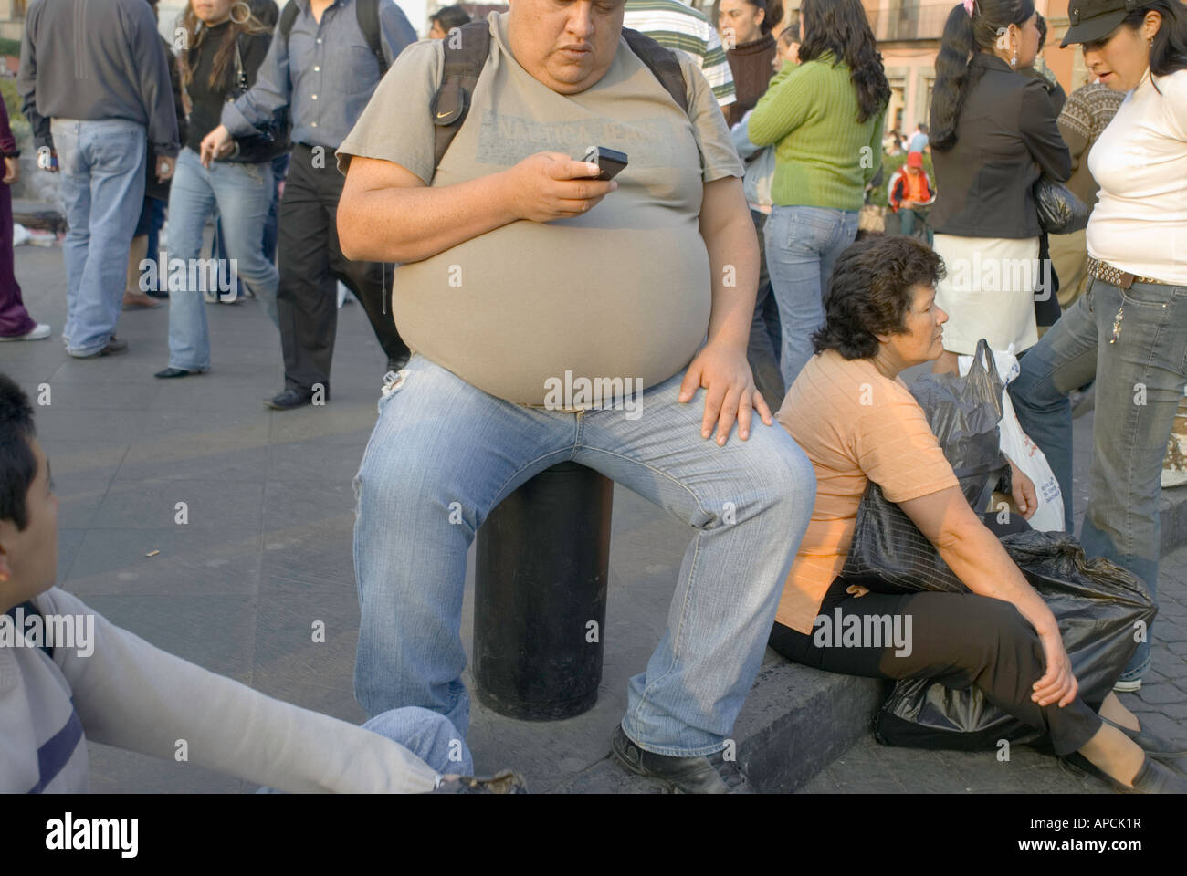An overweight obese man dials his celular phone while seated on a post ...