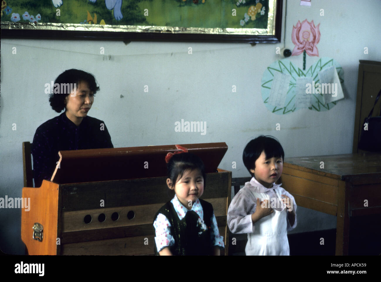 Two young Chinese girls sing with piano assitance from teacher Stock ...