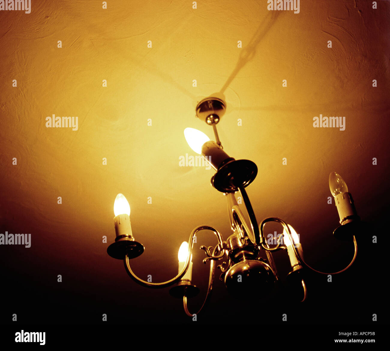 A crooked old chandelier of light bulbs hangs from ceiling creating ...