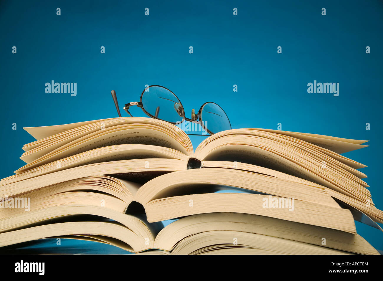 Stack of books with glasses on top, blue backdrop Stock Photo - Alamy