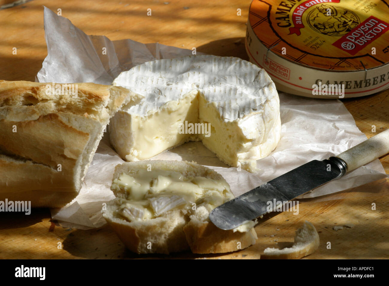 Small Camembert cheese unboxed and cut in rustic setting with bread and ...