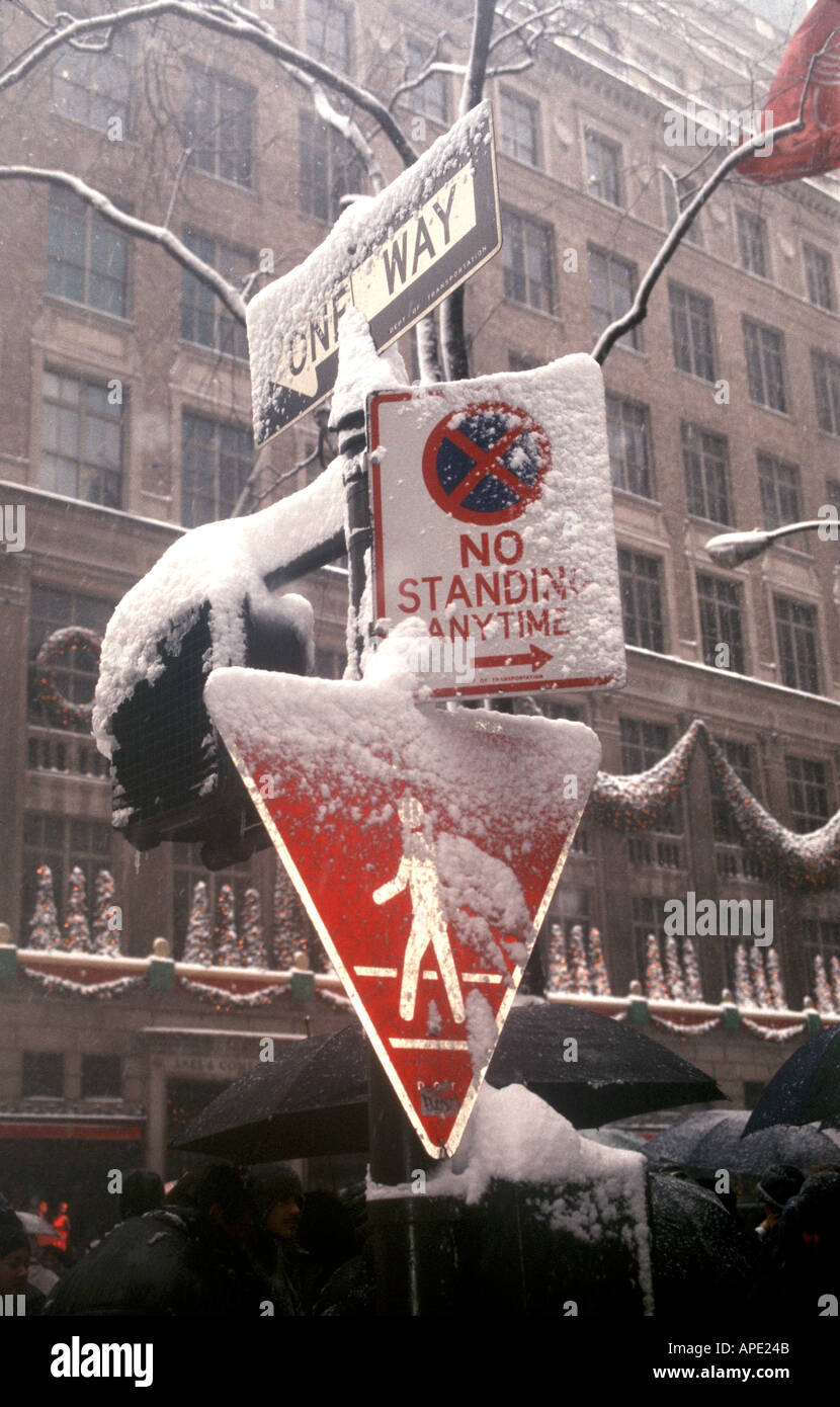 A traffic light pole with traffic signs is covered with snow during a ...