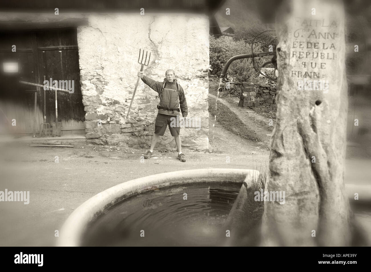 A man walking with a pitchfork in front of an old fountain ...