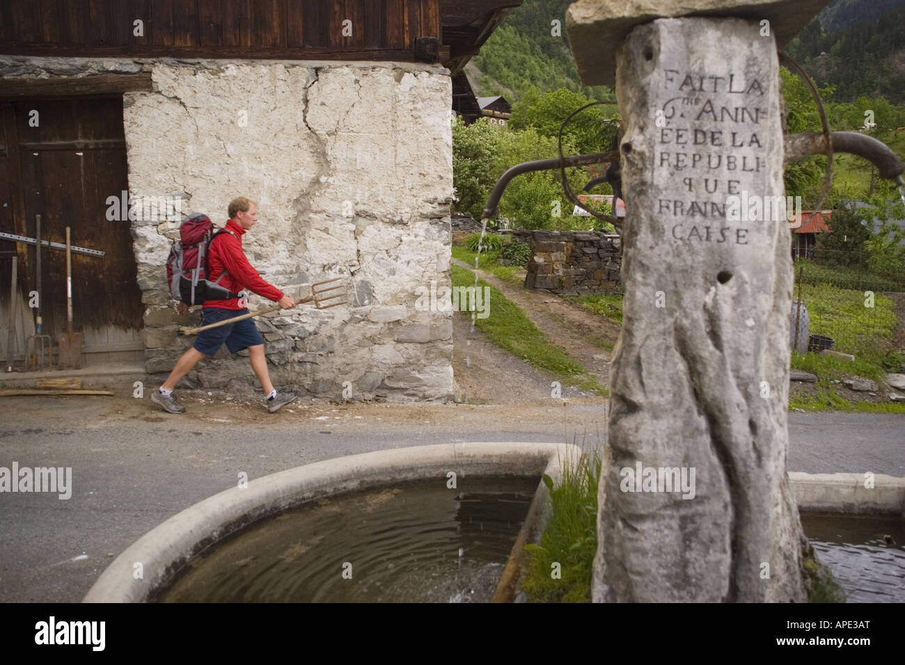 A man walking with a pitchfork in front of an old fountain ...