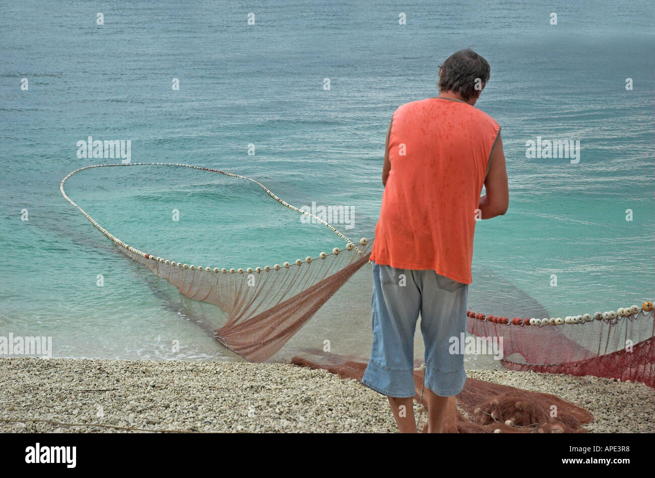 Fisherman on pebble beach puling out fishing net out of ocean water ...