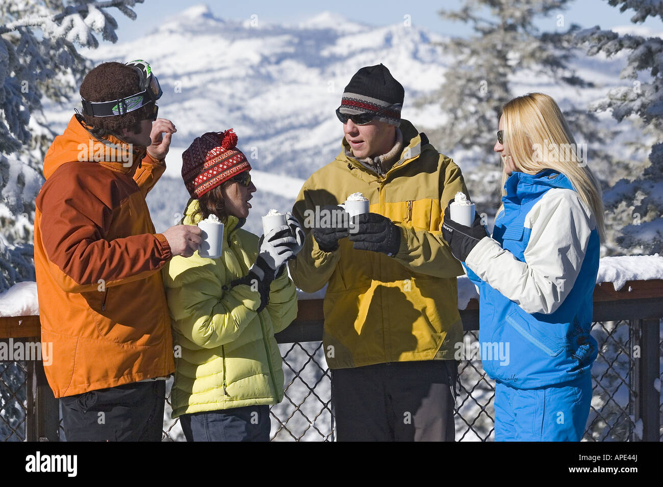 Friends smiling and drinking hot chocolate on a snowy deck in winter at ...