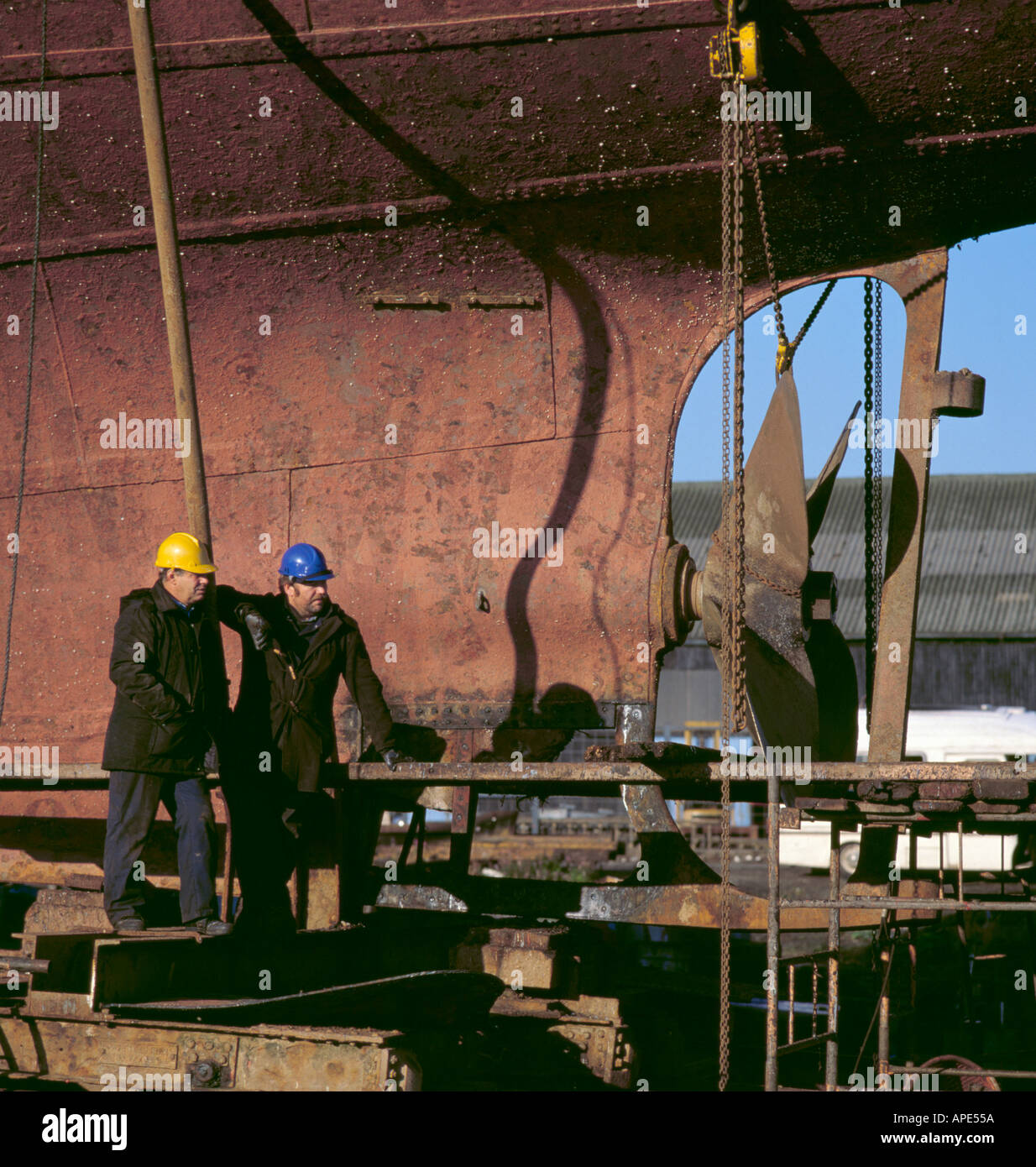 Shipyard scene showing a ships propellor slung from two chain pulleys ...