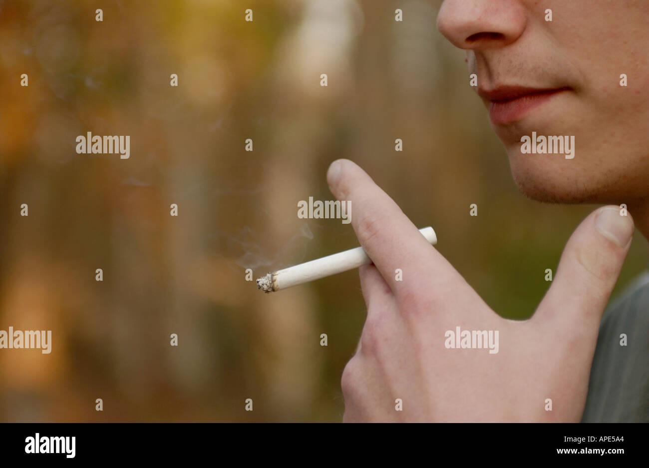 Horizontal color image of a teenage male smoking a cigarette outdoors ...