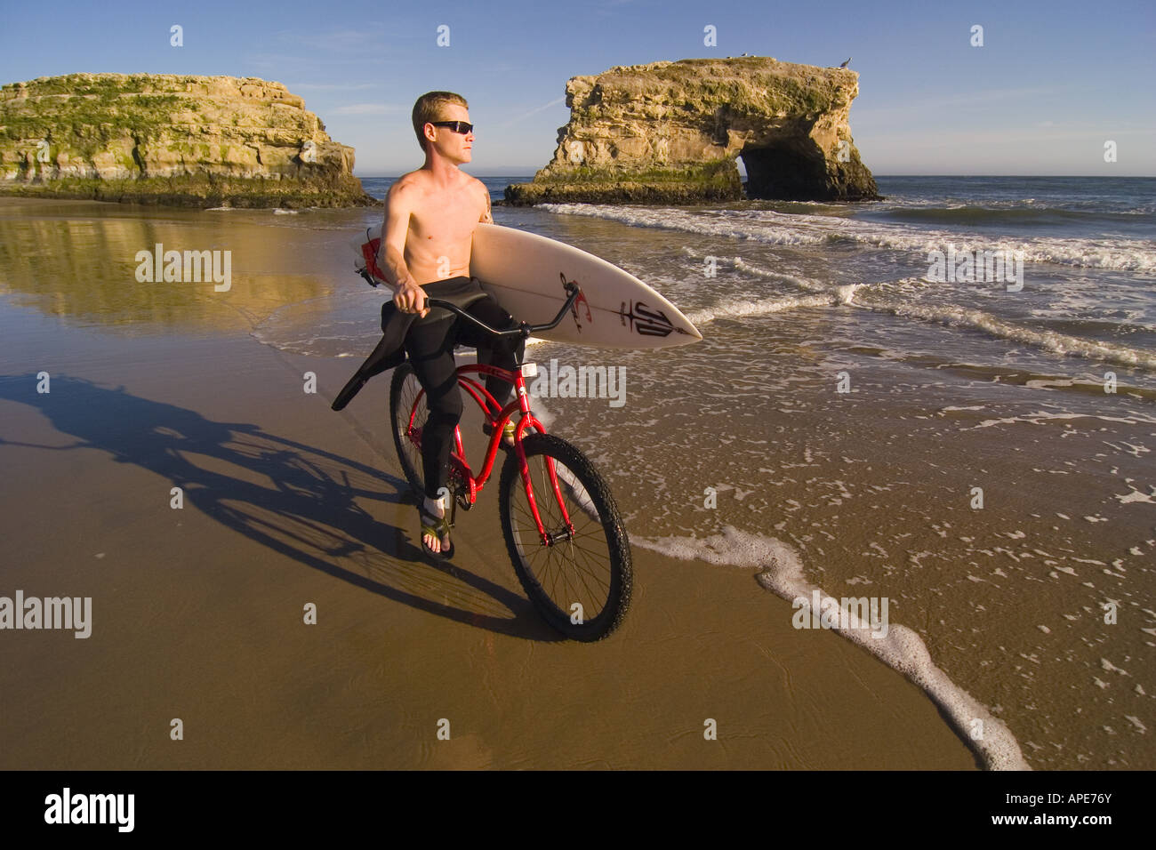 A man with a surfboard riding a cruiser bike on the beach at Natural ...