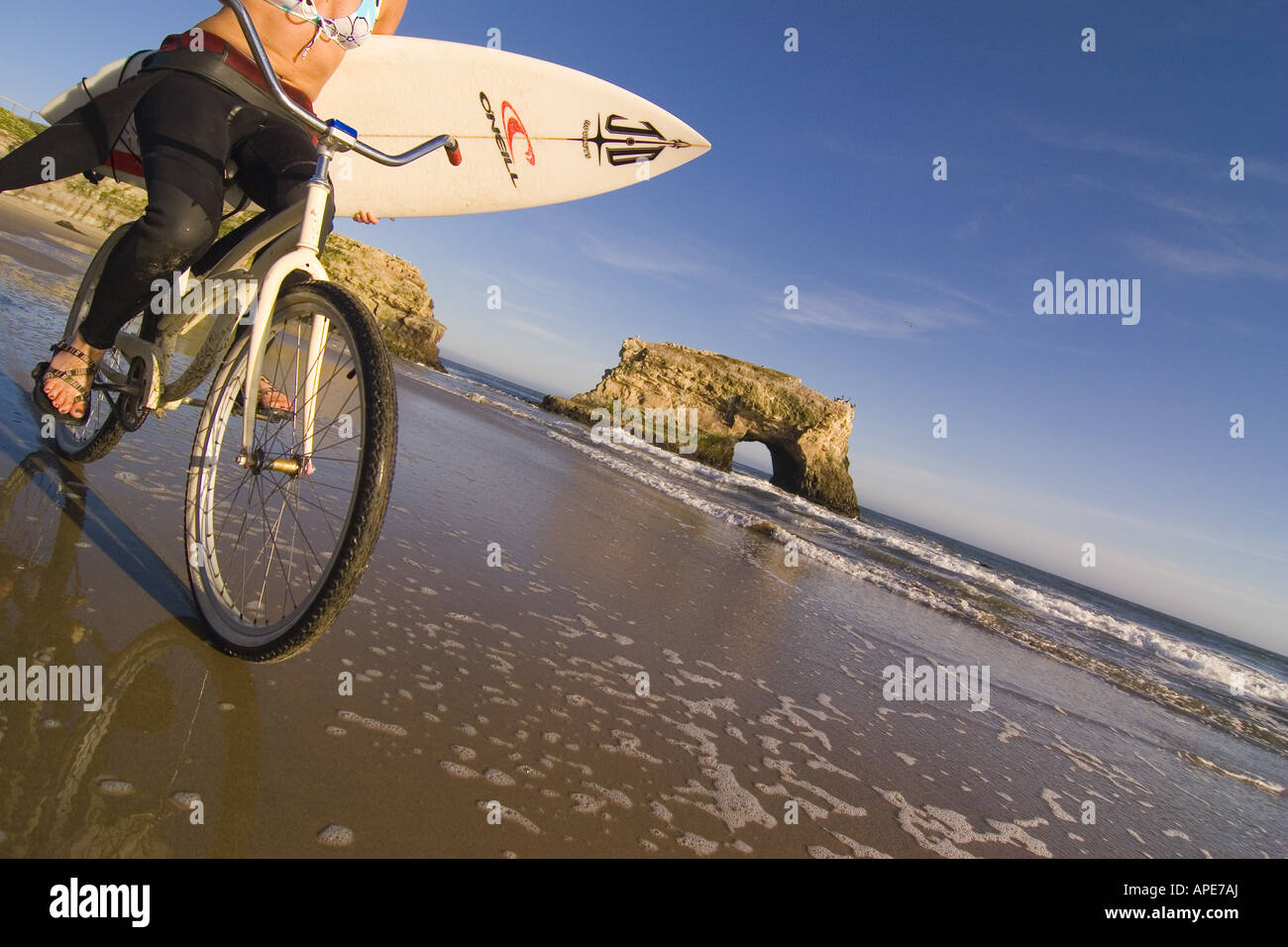 A woman with a surfboard riding a cruiser bike on the beach at Natural ...