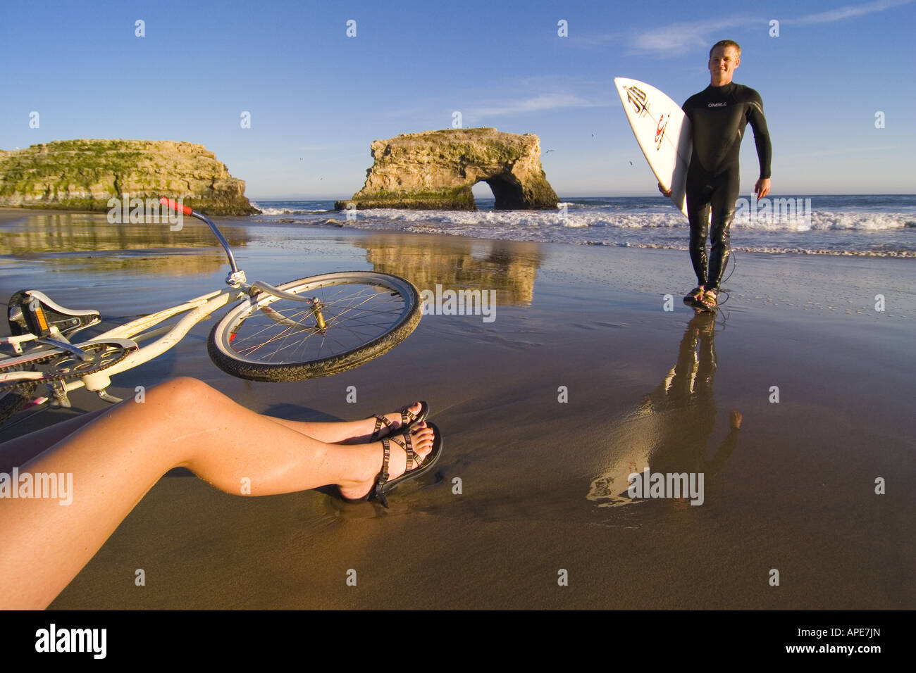 A woman's legs, a surfboard, a bike and a surfer at the beach at ...