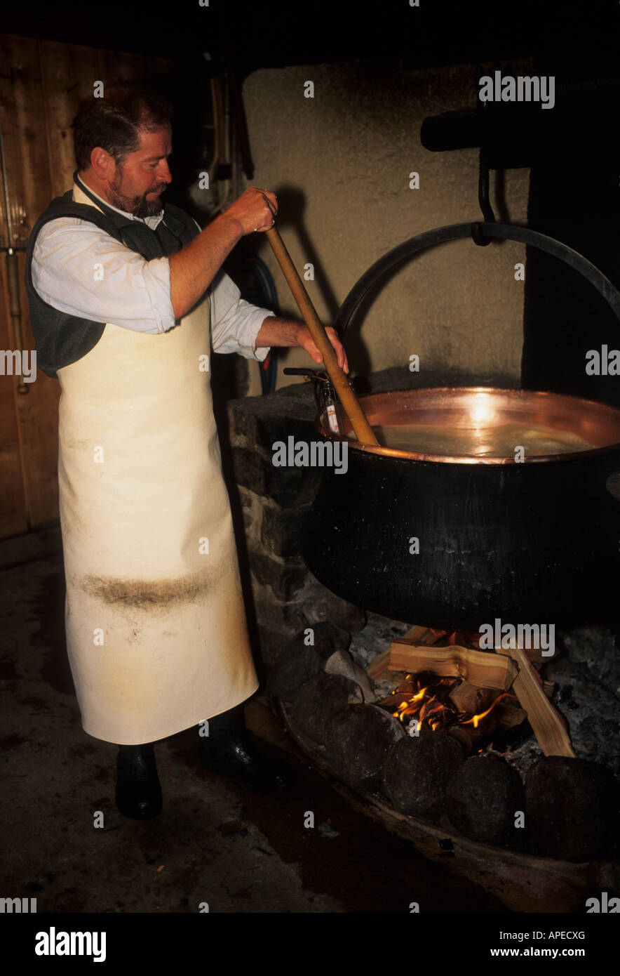 A cheese maker stirs milk in a pot in traditional cheese making farm ...