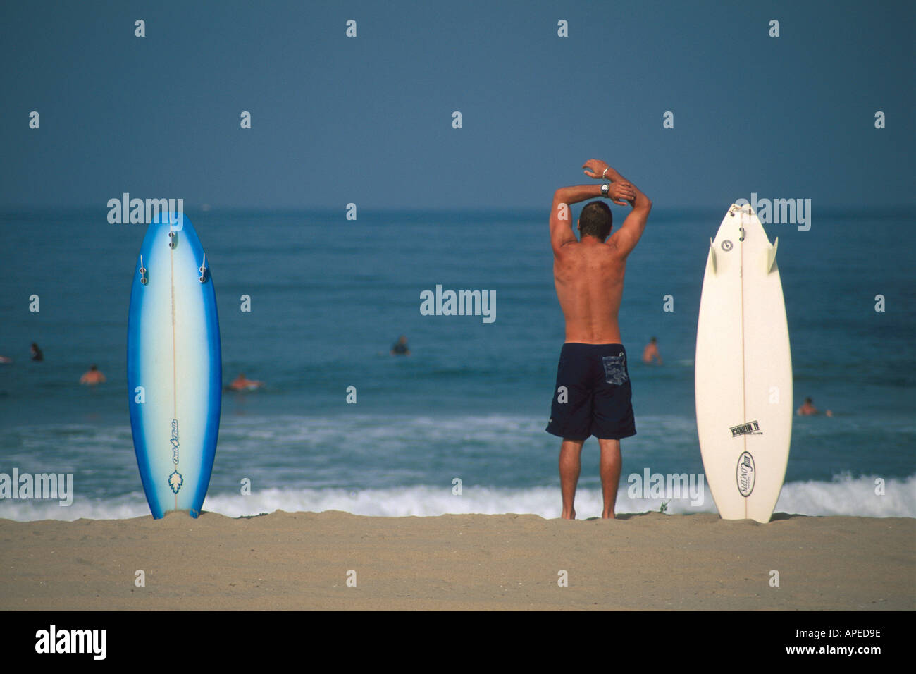 Surfer streching arms bac and surboard on sand beach in front of ocean ...