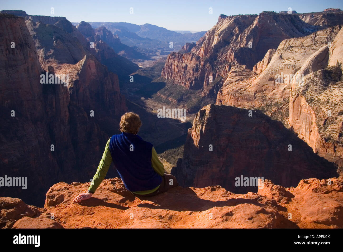 A man looks down the valley with his feet hanging over the cliff edge ... A man looks down the valley with his feet hanging over the cliff edge ...