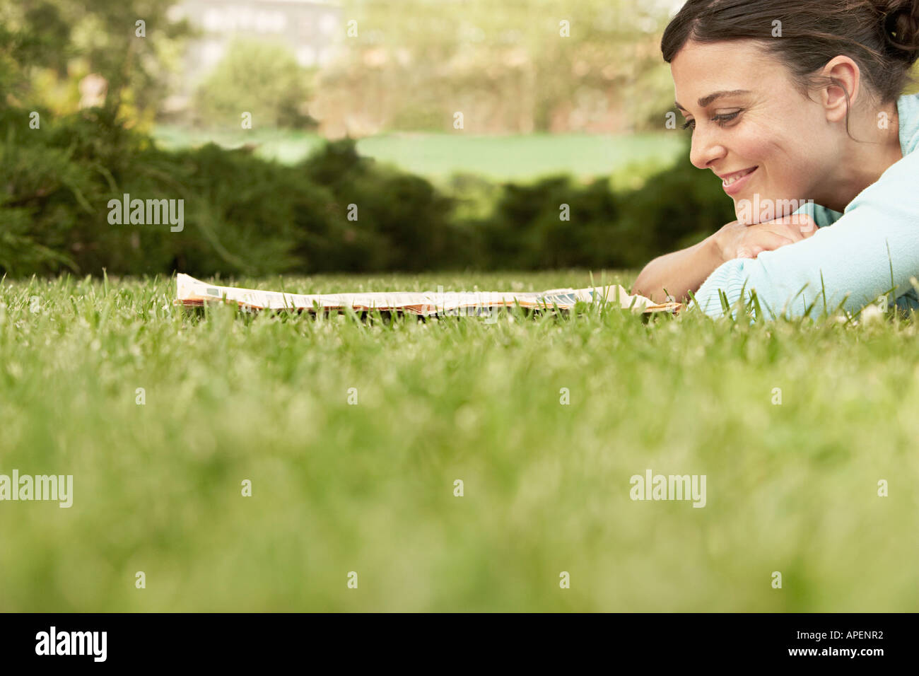 Woman lying on grass, reading newspaper, side view Stock Photo - Alamy