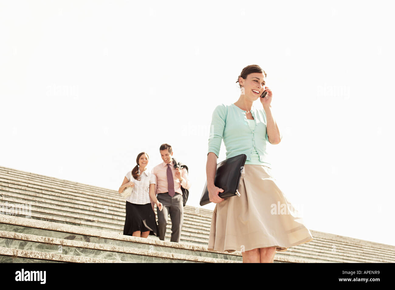 Three office workers walking down steps, woman in foreground using ...
