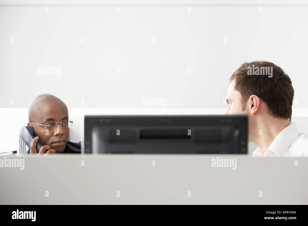 Two office workers sitting in office cubicle, one using phone Stock ...