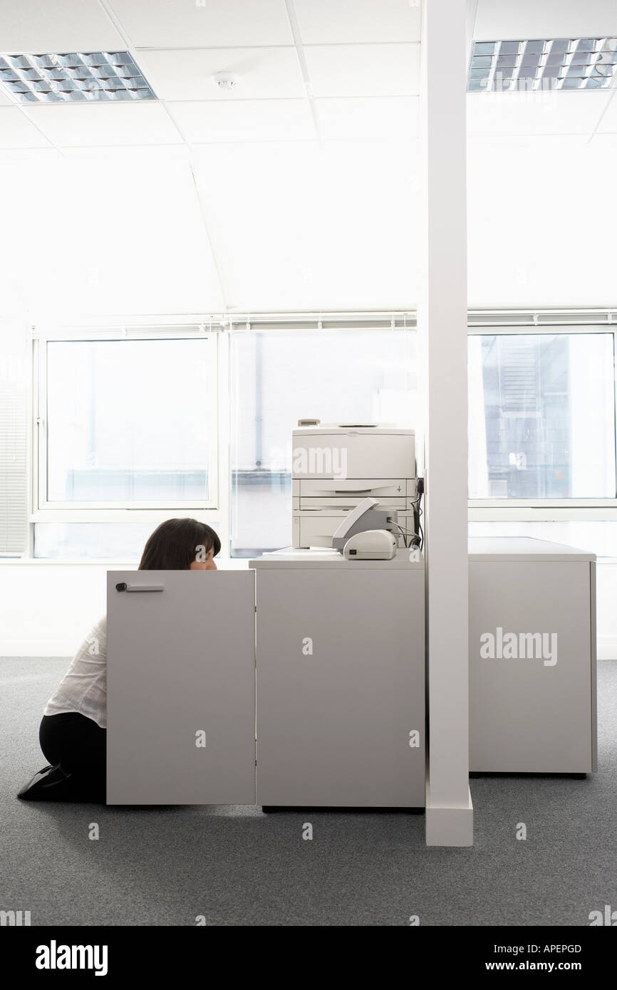 Female office worker kneeling in front of open cabinet in office, side ...