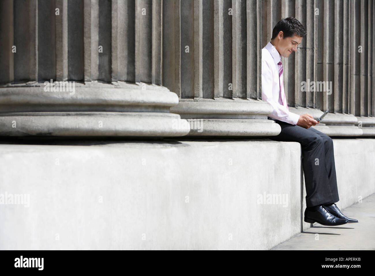 Businessman sitting between pillars outside building sending text ...