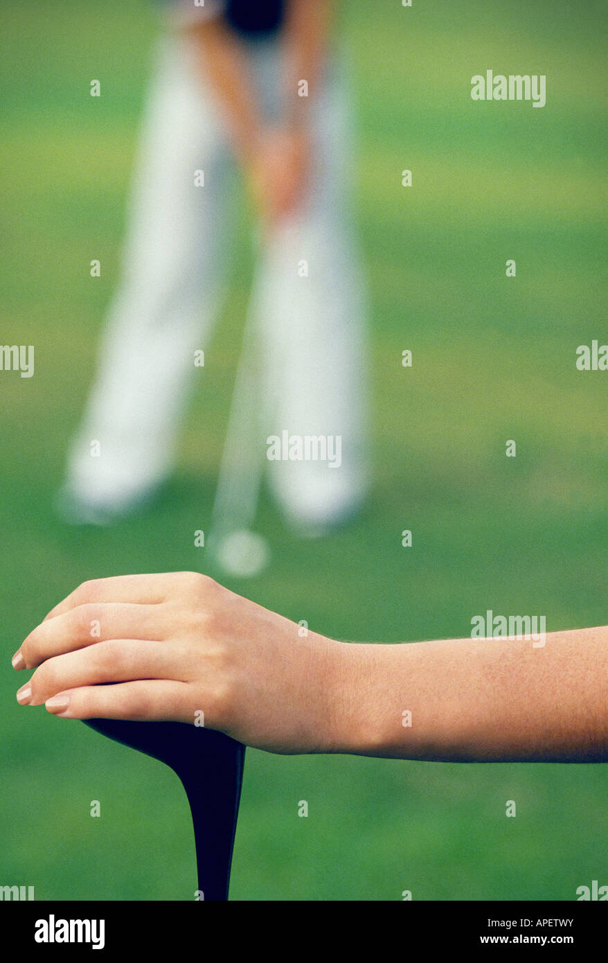 Close-up of woman's hand resting on golf club, man's figure about to ...