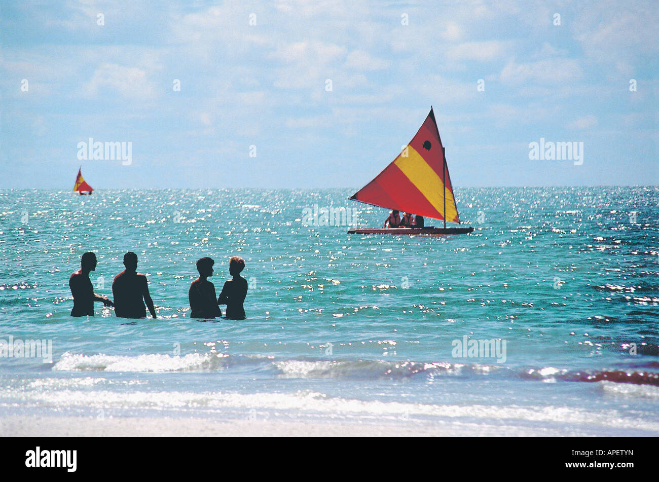 Family in silhouette in waist deep water near beach with sailboard in ...