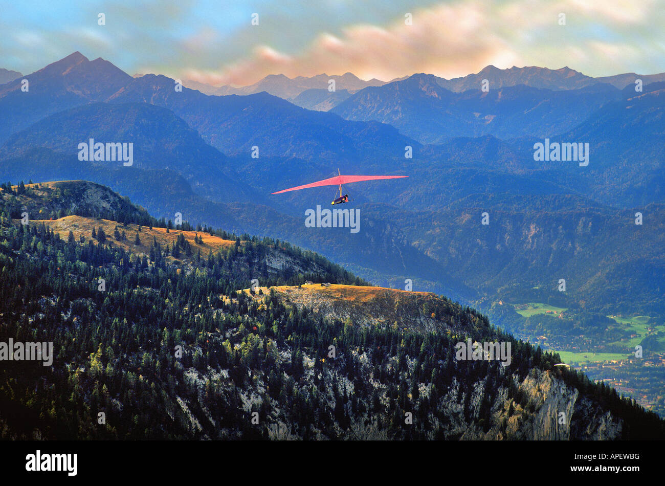 Parasailer soaring above green valley and mountains with sunset in ...