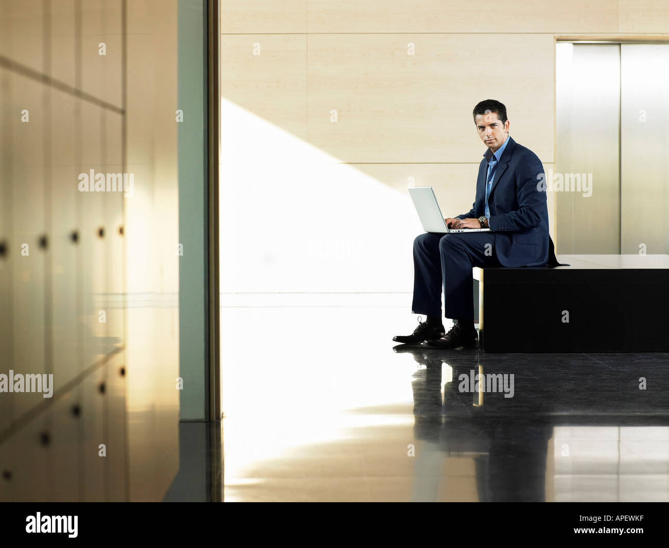 Businessman sitting on bench by elevator using laptop Stock Photo - Alamy