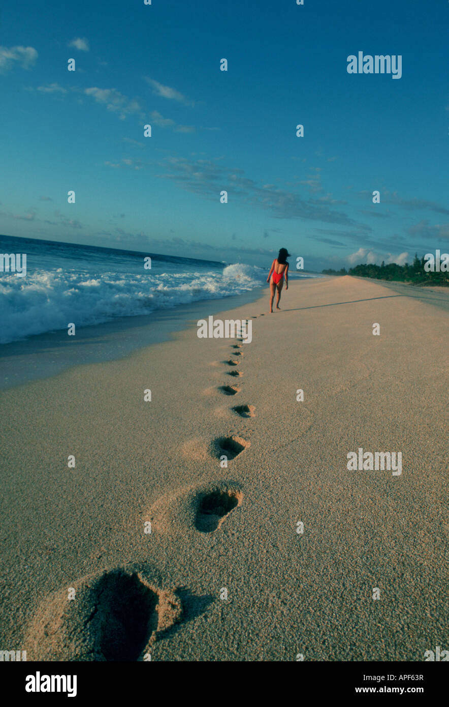 Woman walking in the distance leaving behind her footprints in the sand ...