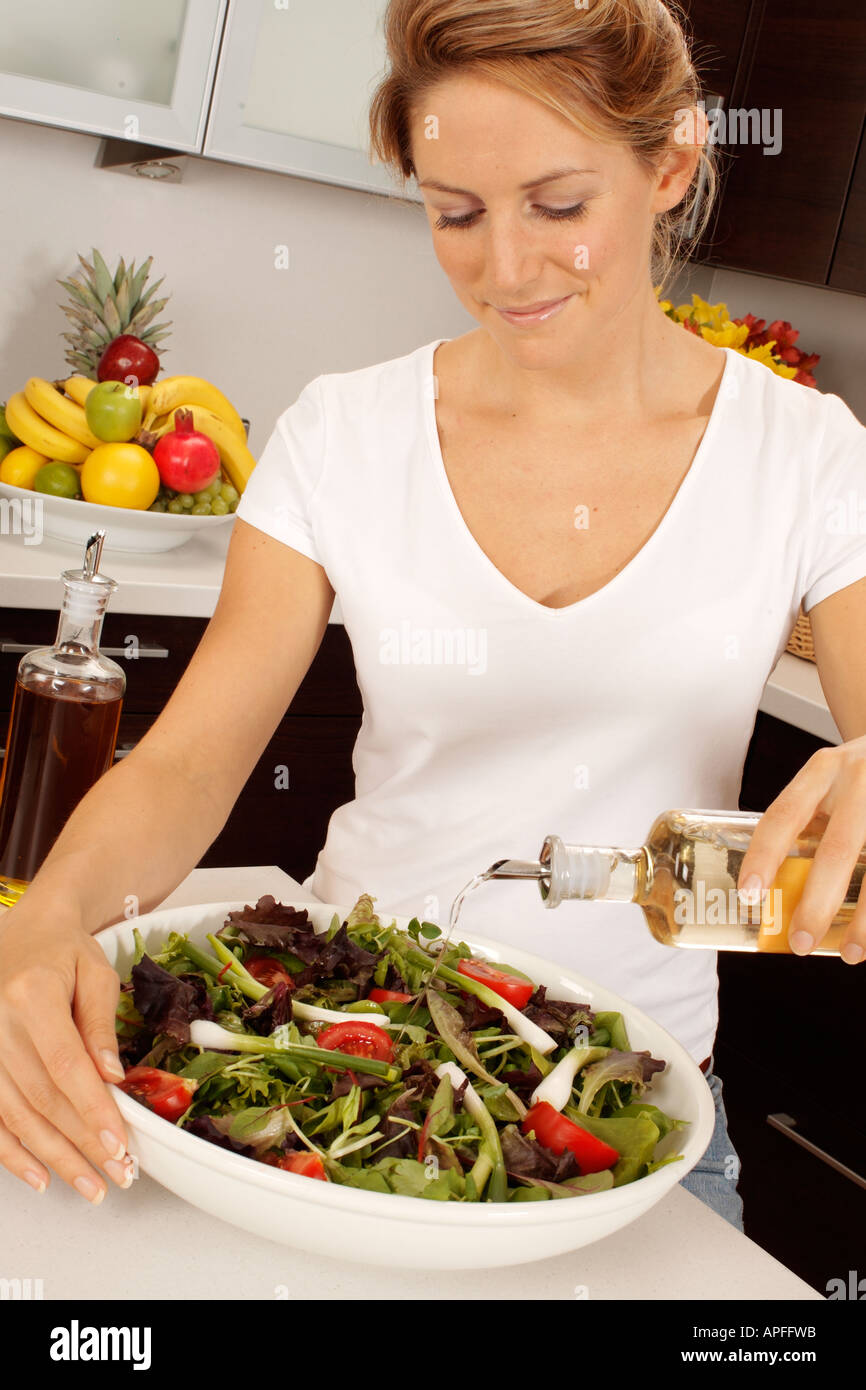 WOMAN IN KITCHEN POURING SALAD DRESSING ON SALAD Stock Photo - Alamy