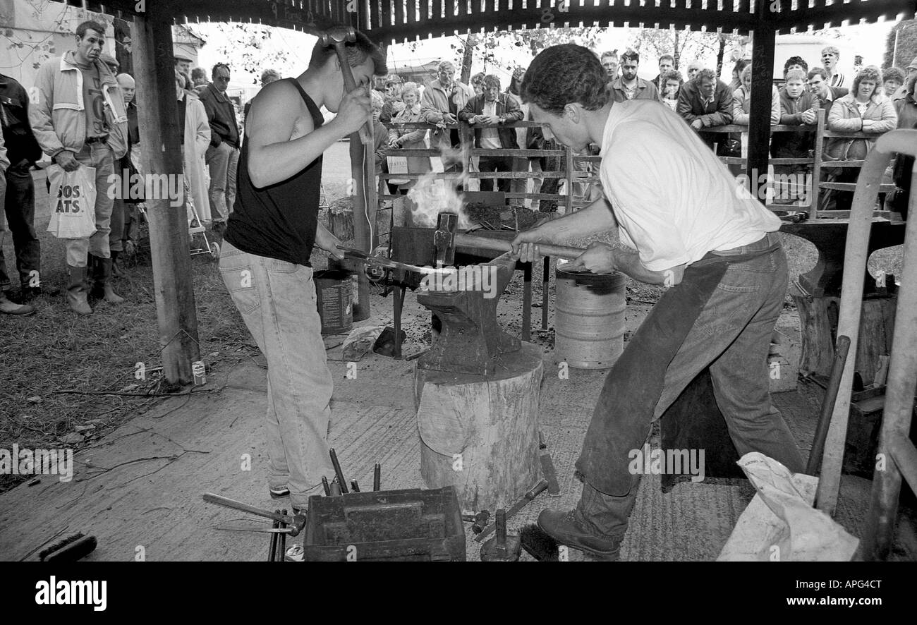 Two young blacksmiths giving demonstation of hammering hot iron bar ...