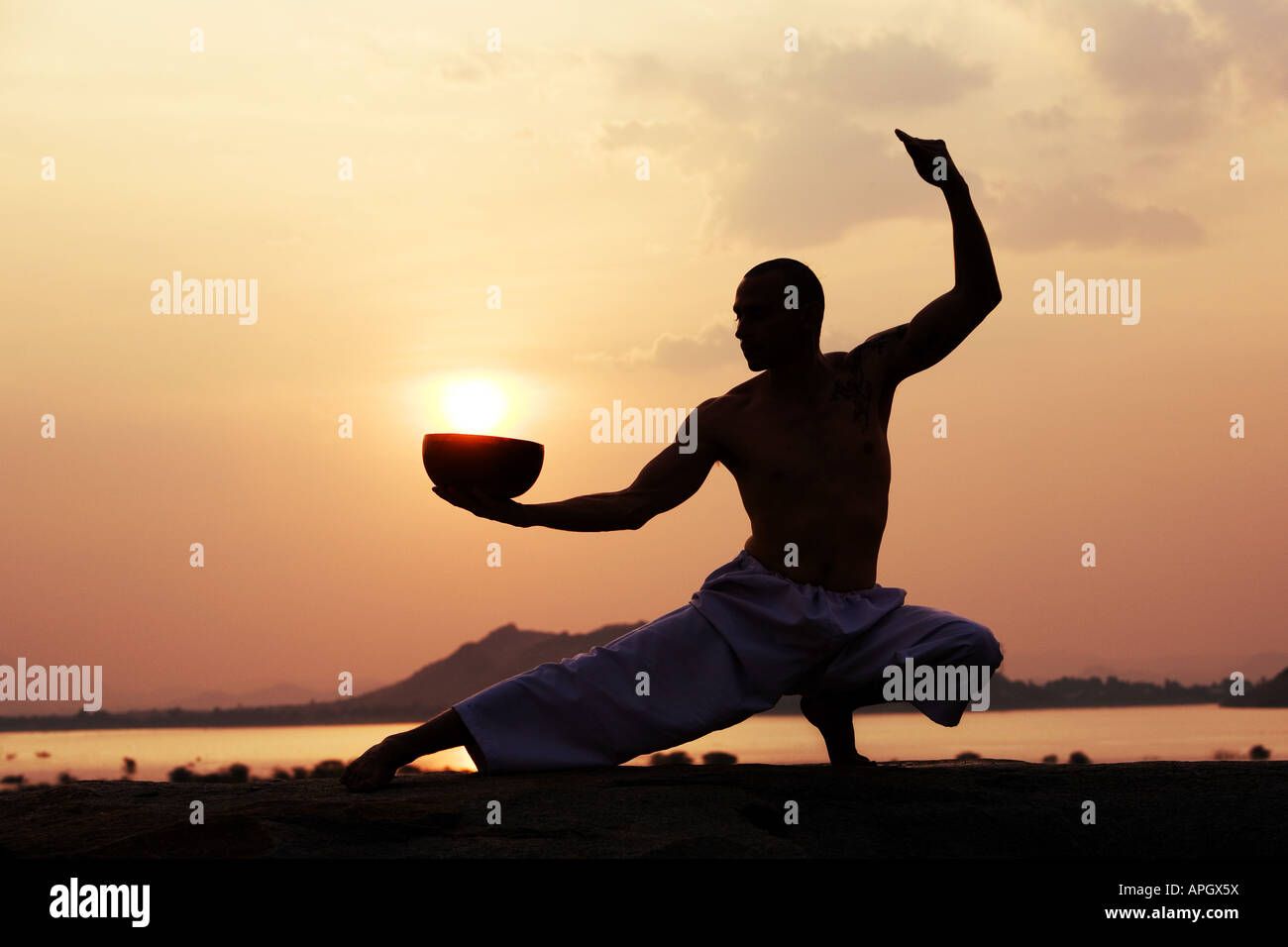 Man performing tai chi with Tibetan singing bowl against a setting sun ...