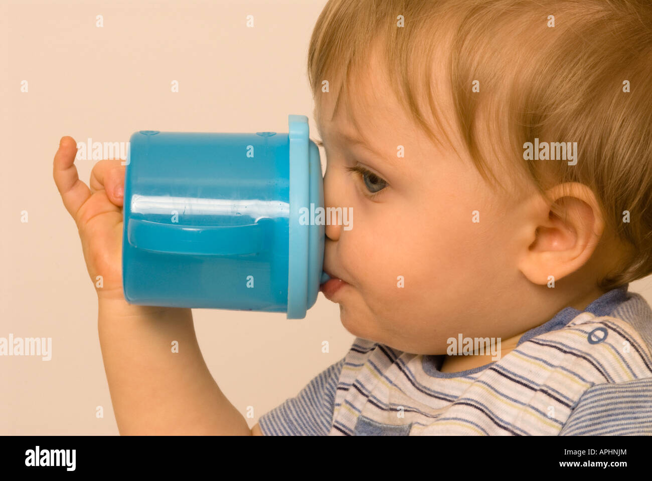 Baby boy eleven months old drinking whilst holding his own drinking cup ...