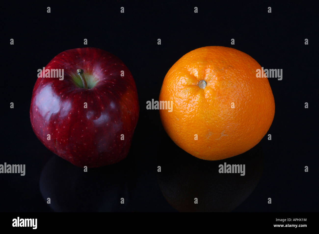 red apple and orange side by side shot in studio on black background ...