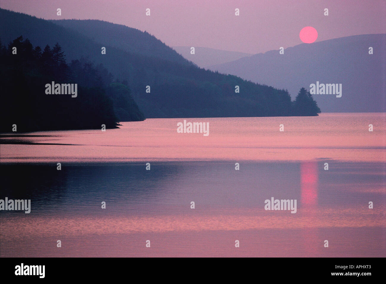 A red sun setting over Lake Vyrnwy with wooded hills behind Powys Stock ...