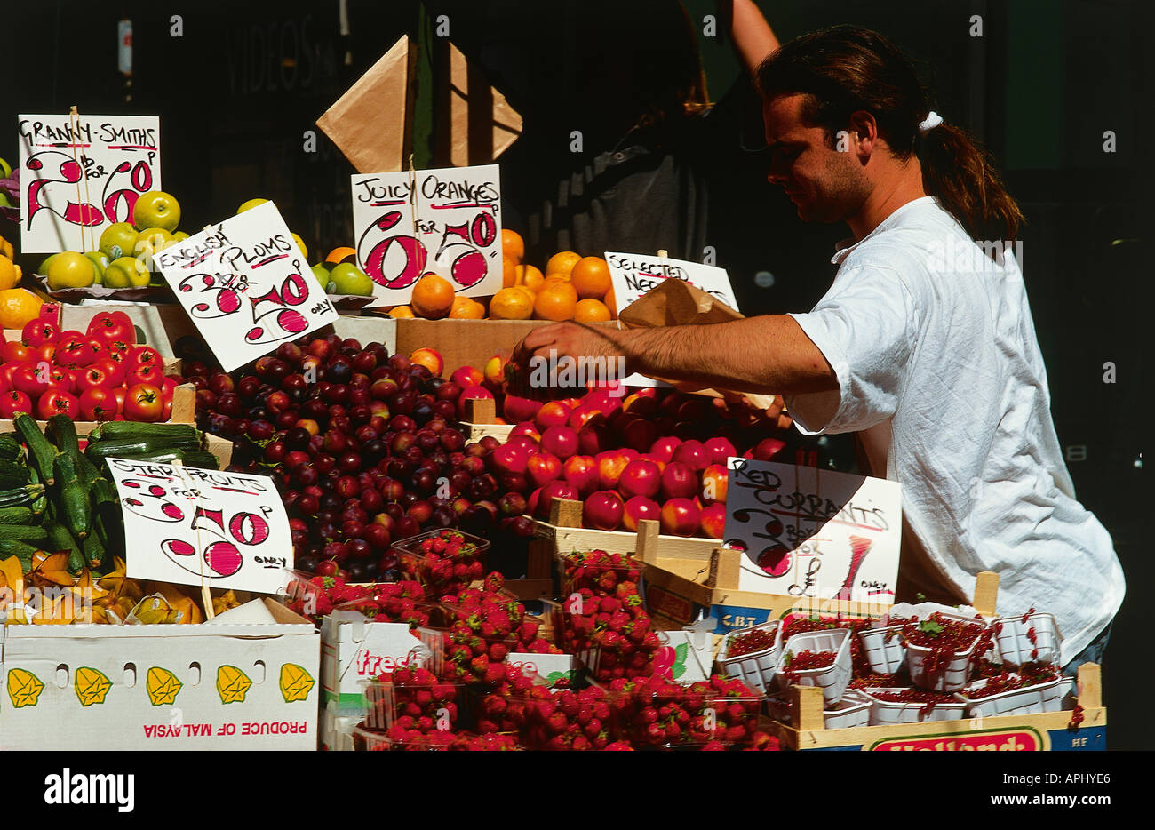 A vendor in front of a colourful stall selling fruit in Portobello Road ...
