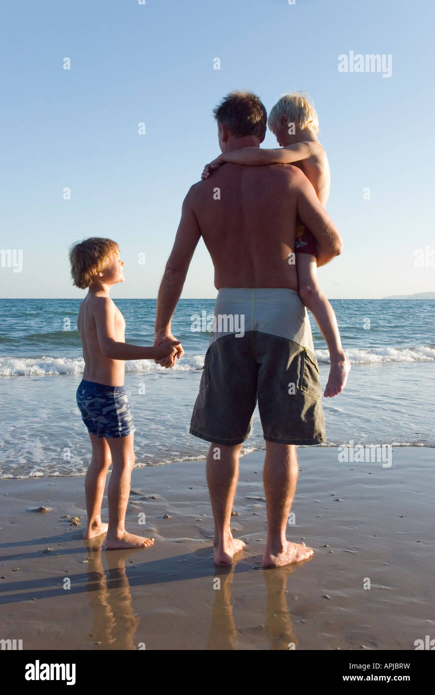 A colour portrait of a father with his two young sons on the beach in ...