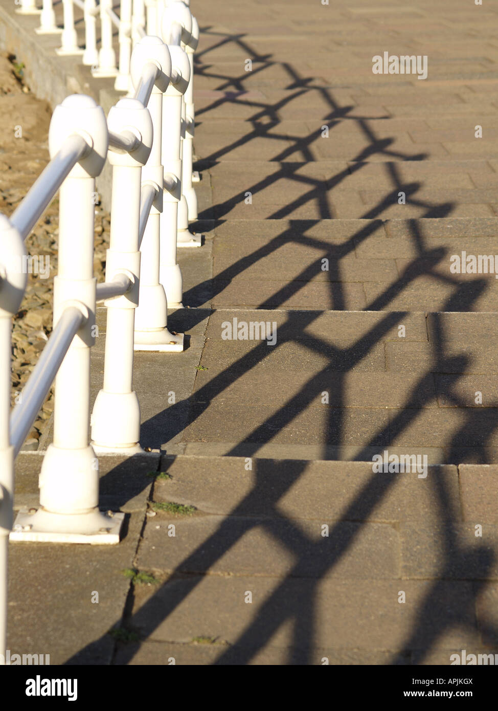 Shadow s from white metal beach side railing, lying across stone steps ...