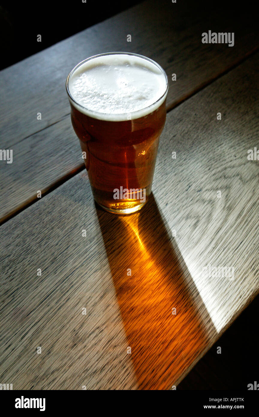 A pint of bitter standing on an old wooden table in an English pub ...